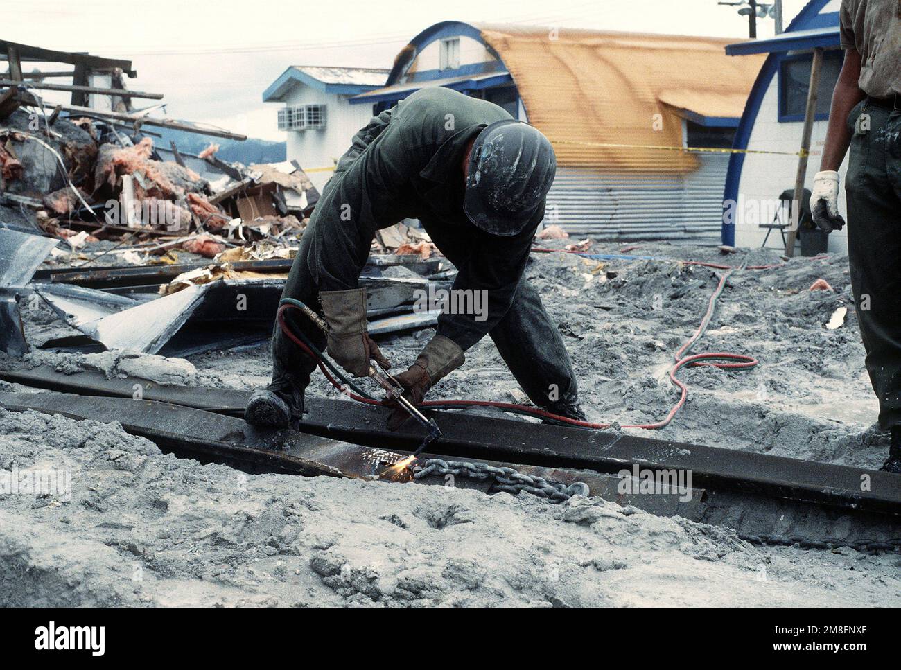 A Seabee uses a cutting torch to cut through an I-beam in the rubble of ...
