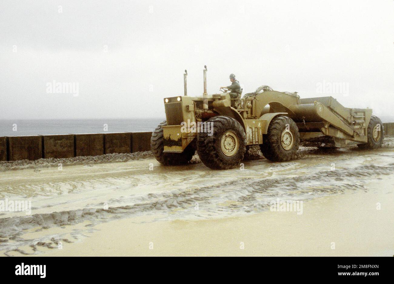 A Seabee drives a motorized earthmoving scraper along a road being ...