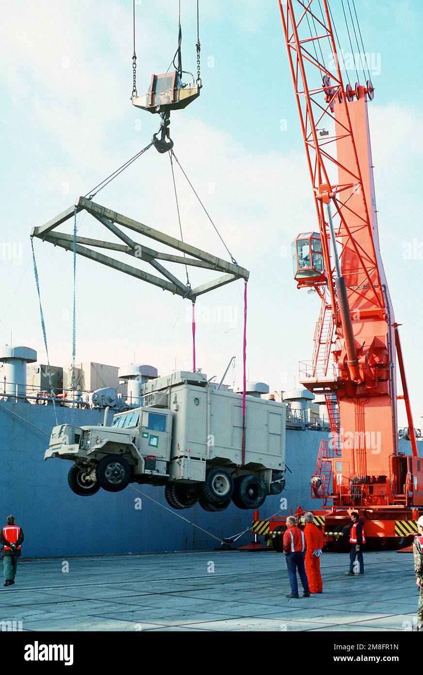A crane lowers an M-809 5-ton truck with van body to the pier as ...