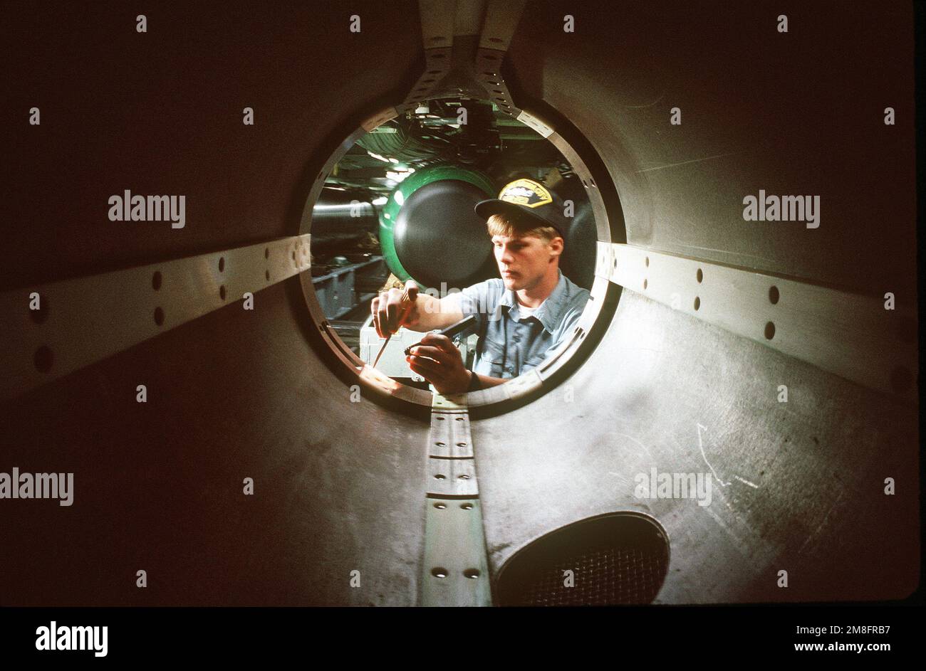 A crew member performs routine maintenance on a torpedo tube aboard the ...