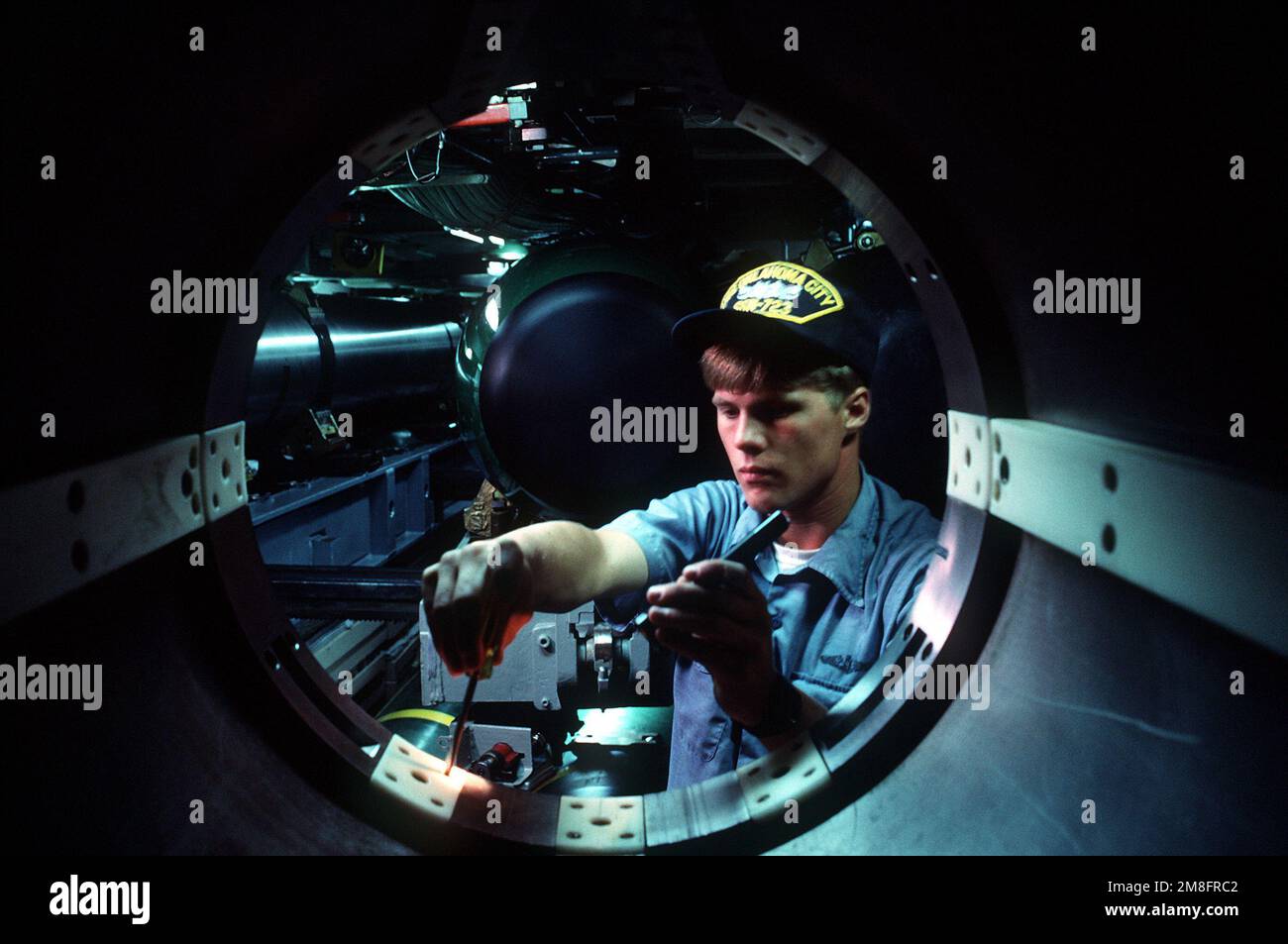 A crew member performs routine maintenance on a torpedo tube aboard the ...