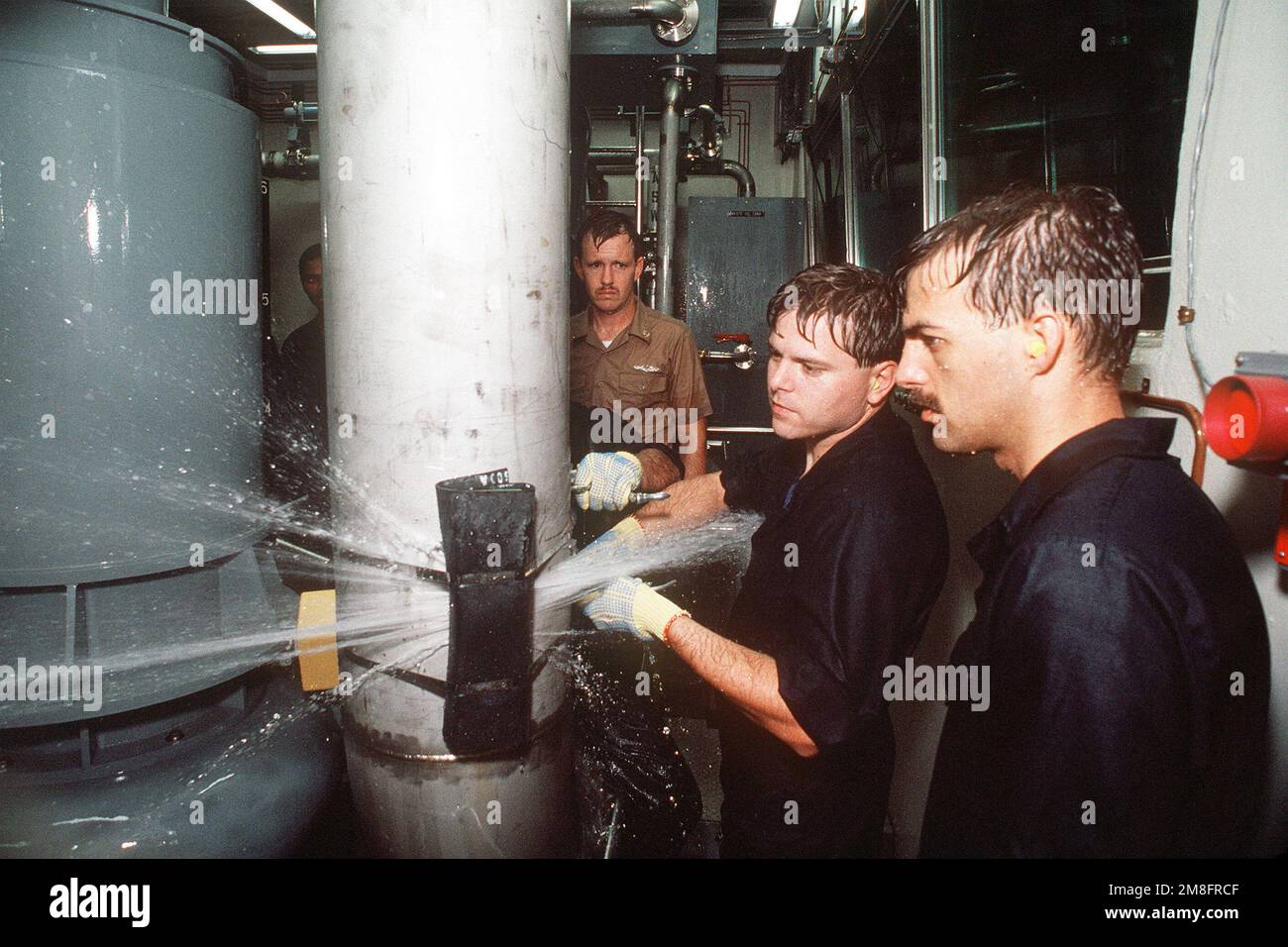 Crew members attach a temporary patch to a leaking pipe in a submarine ...