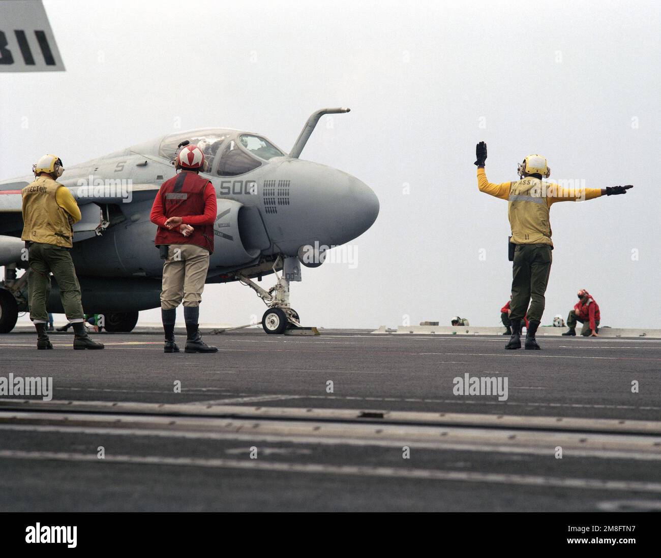 A flight deck crew member signals to the pilot of an A-6E Intruder ...