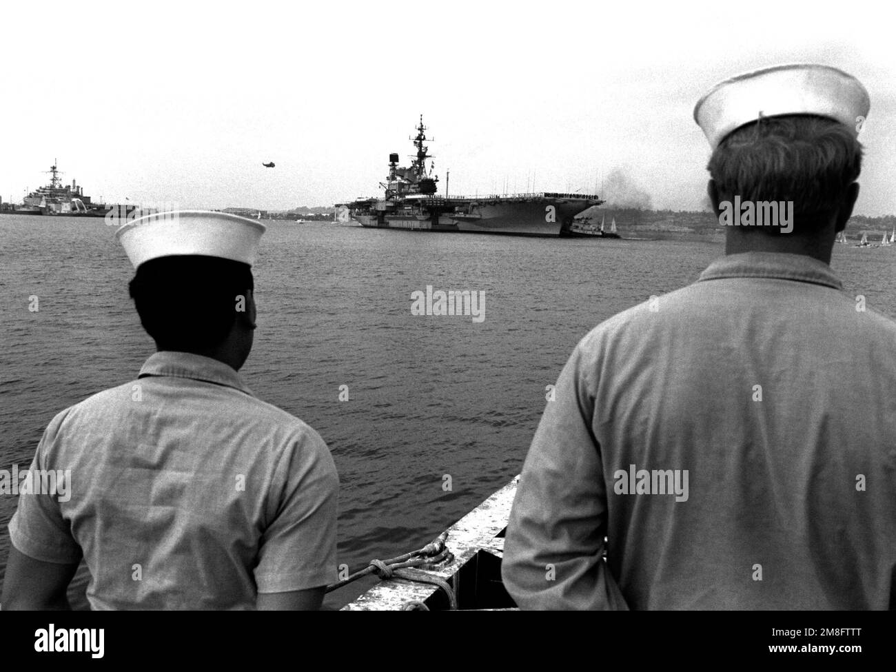 Line handlers stand by on the pier as a tug boat helps maneuver the ...