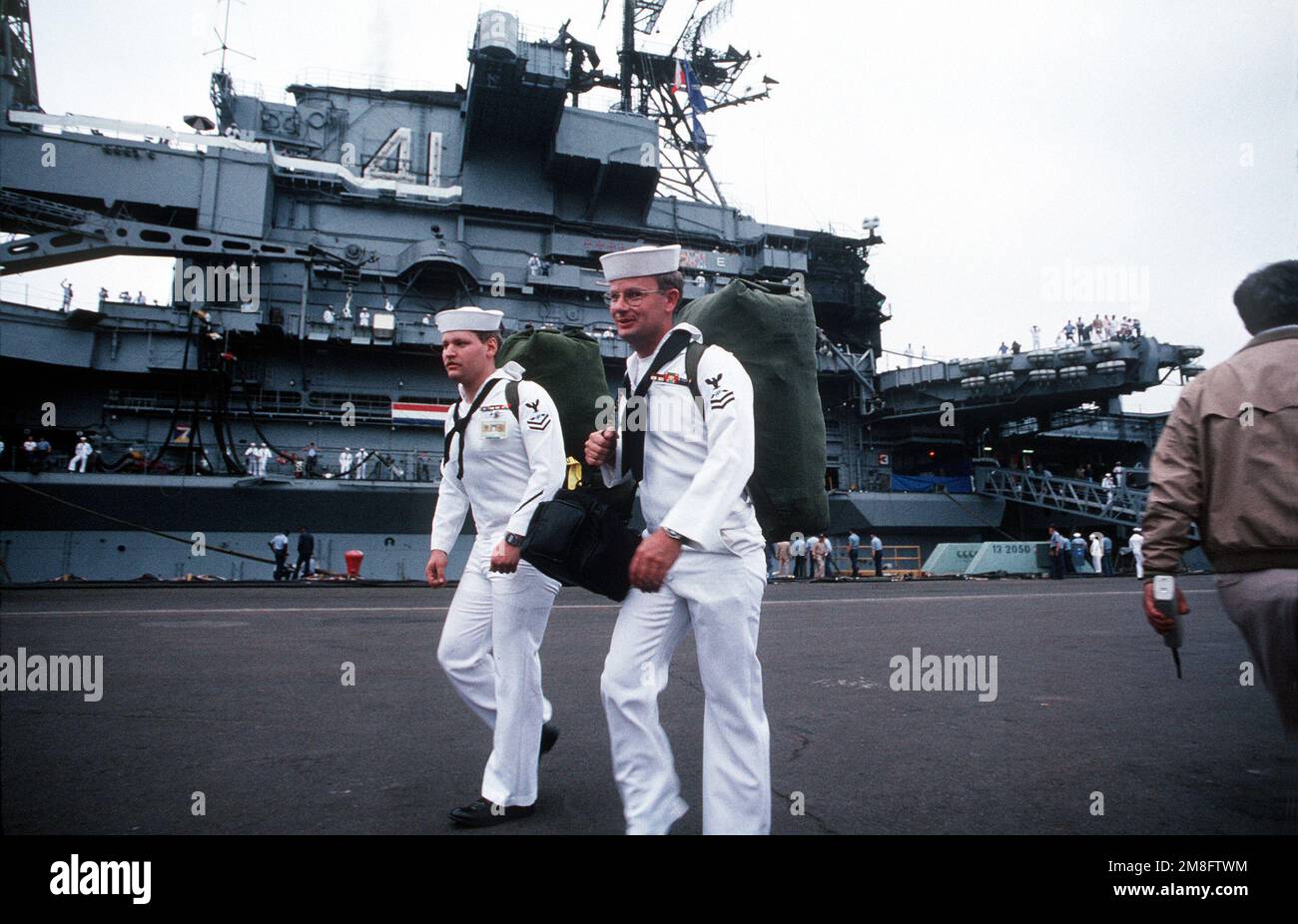 Two petty officers walk across the pier after arriving at the air ...