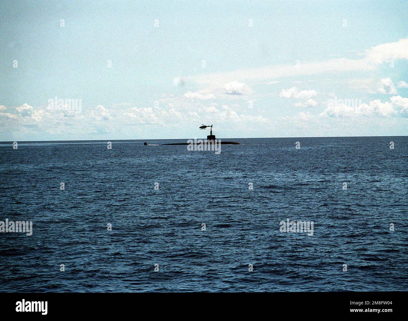 A helicopter passes over the nuclear-powered attack submarine USS ...