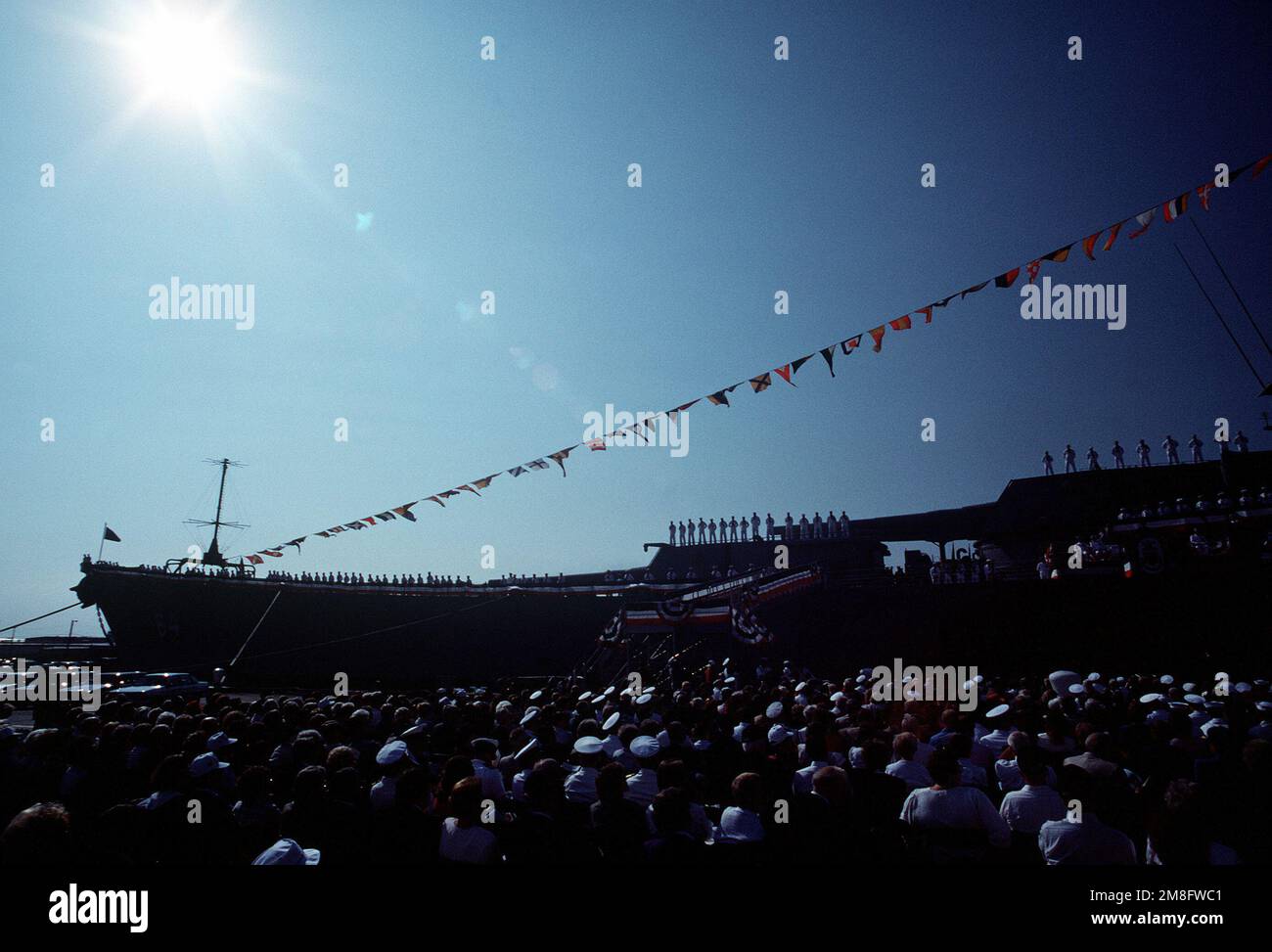 A large crowd watches as crew members man the rails aboard the ...