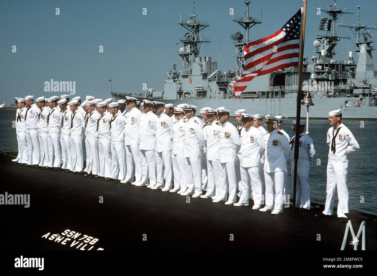 Officers and enlisted men stand at parade rest near the stern of the ...