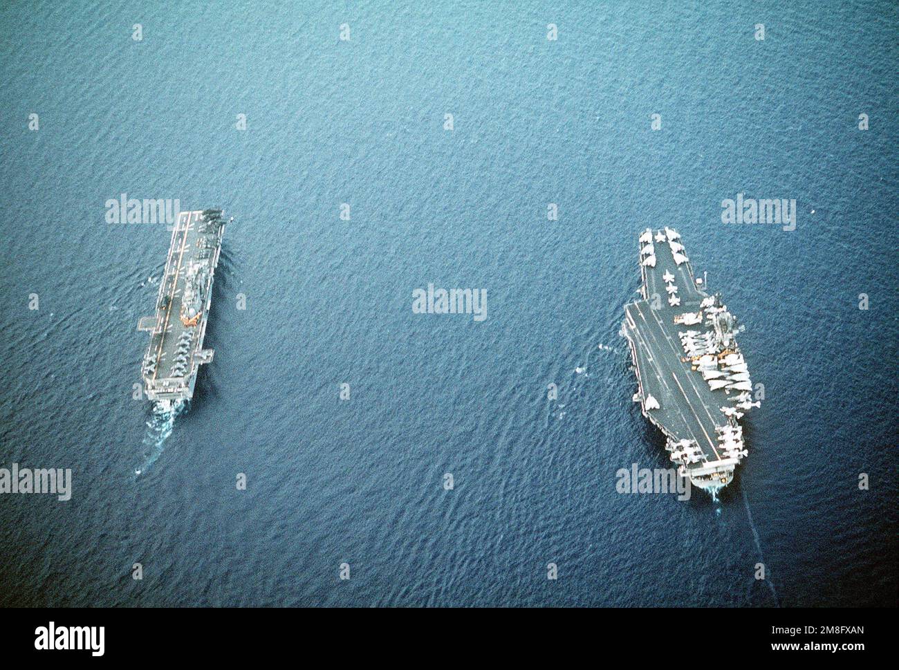 An aerial stern view of the amphibious assault ship USS WASP (LHD-1), left, and the aircraft ...