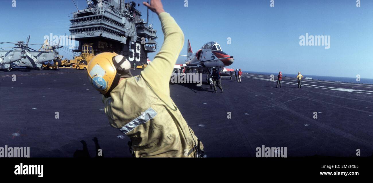 A flight deck director guides an aircraft handler as he steers a ...