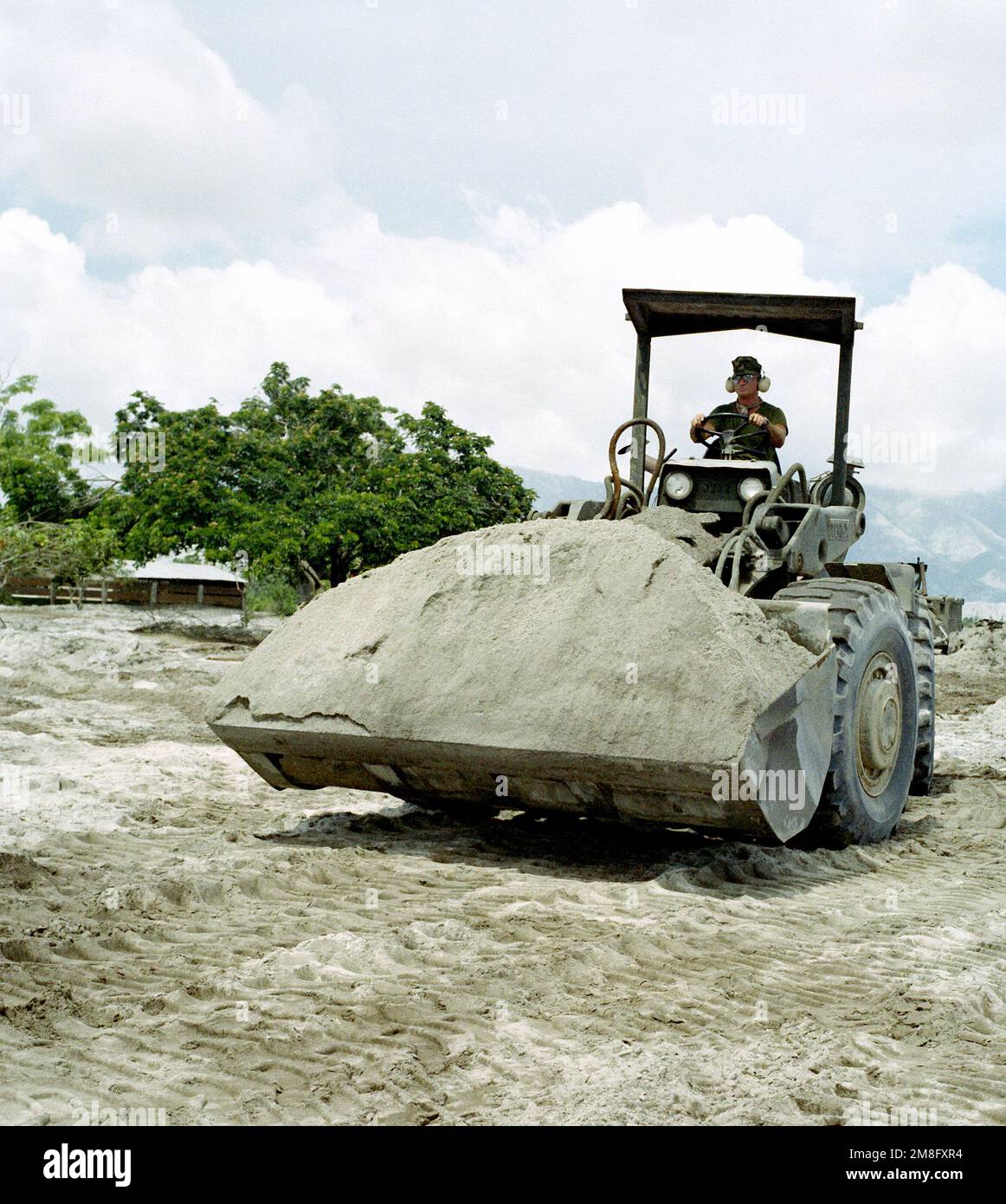 A Seabee operates a front loader while taking part in the cleanup of ...