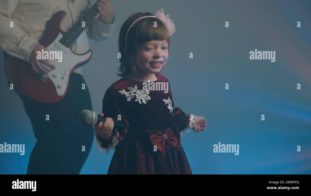 Little girl in vintage dress sings on stage, her father plays an ...