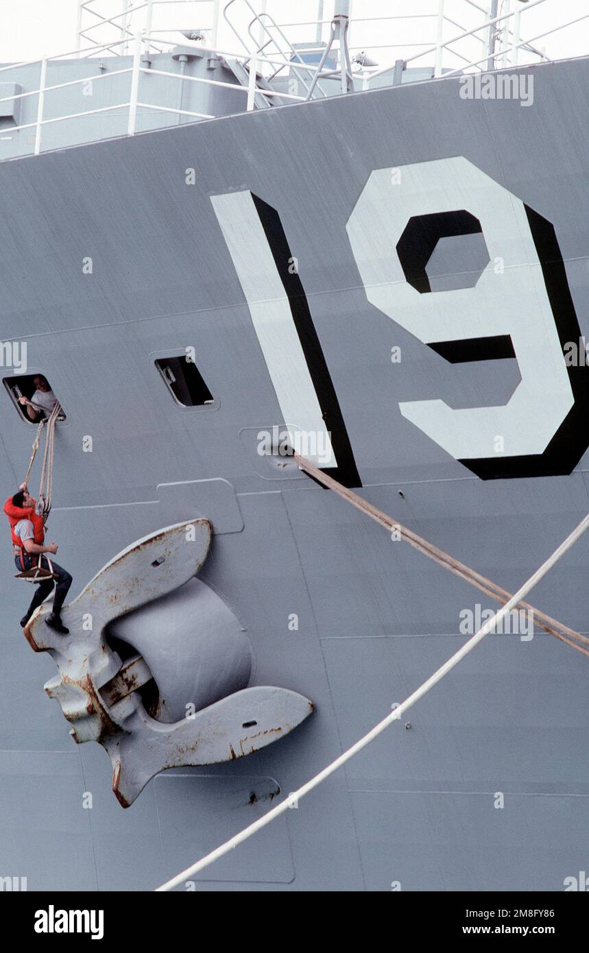A crew member balances himself on the anchor of the amphibious command ...