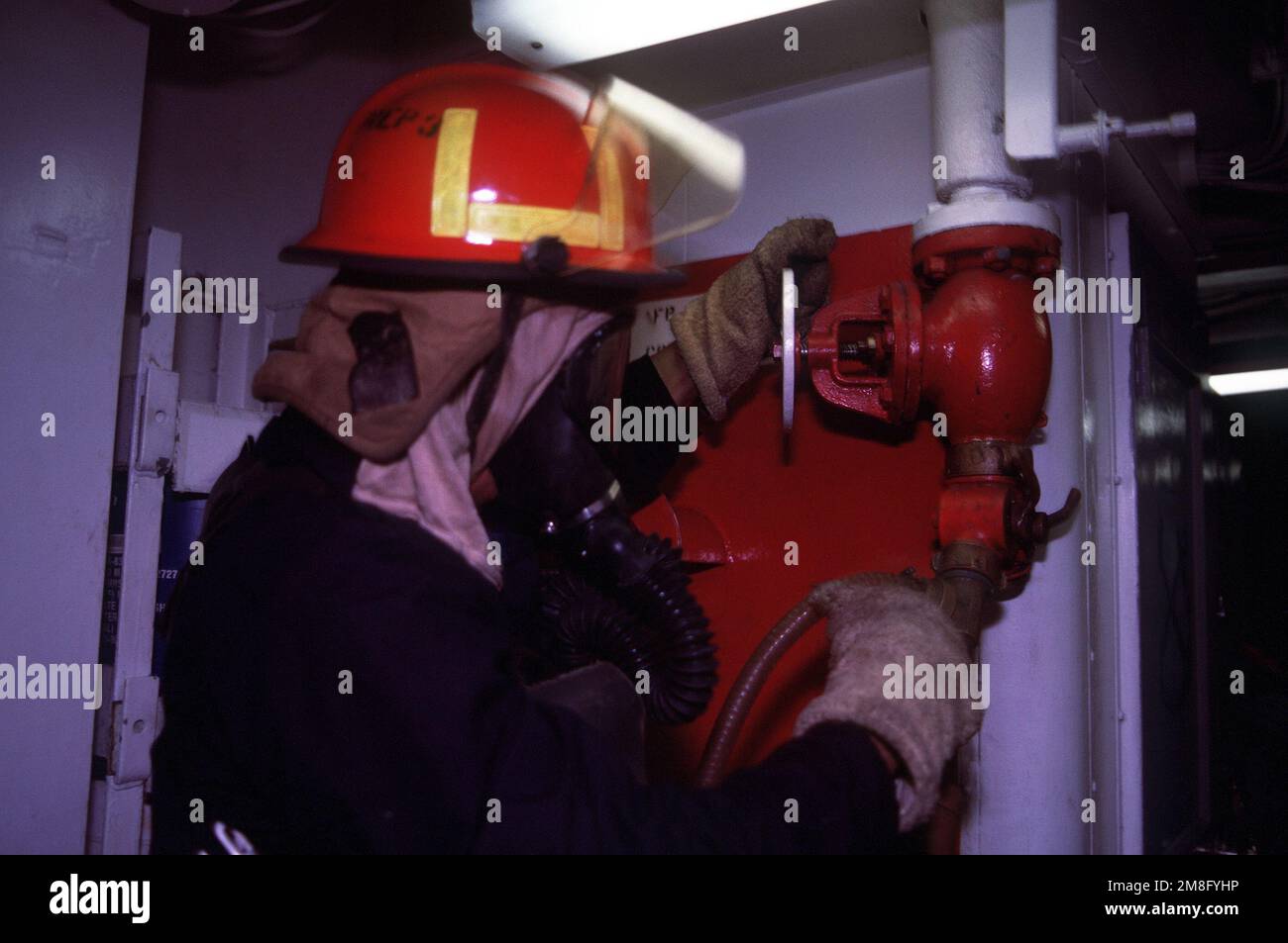A crewman, wearing an oxygen breathing apparatus (OBA), attaches a hose ...