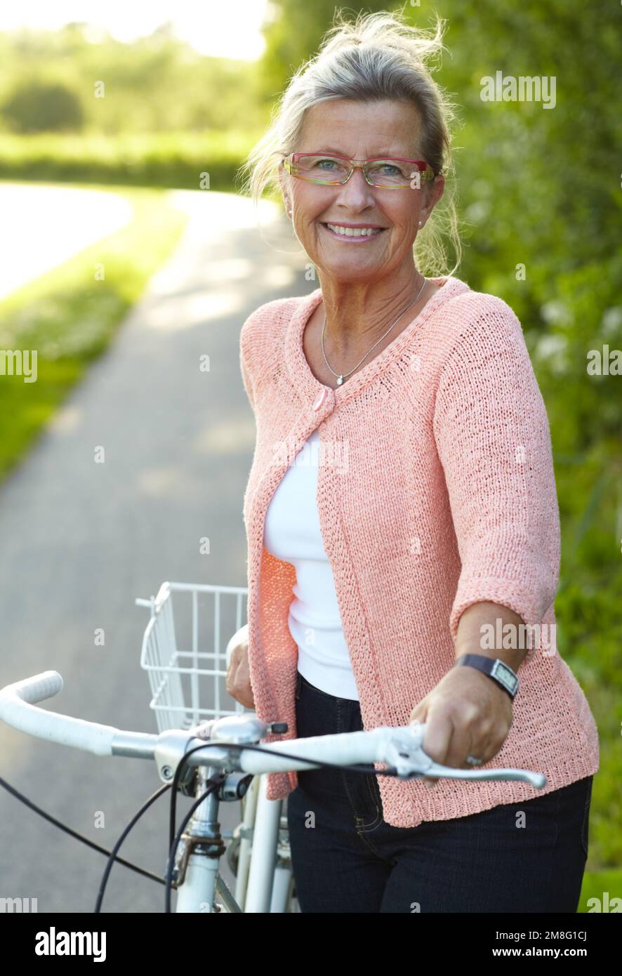 Going for a bike ride on a great day. Smiling senior woman standing on ...