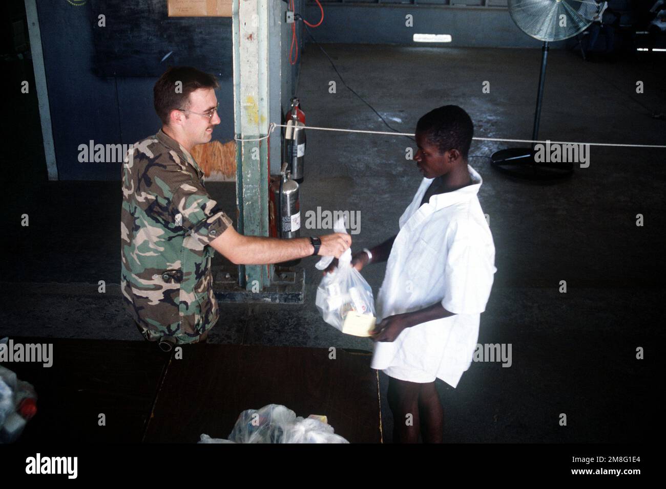 A member of the U.S. Army hands out "basic needs" packages at Camp ...