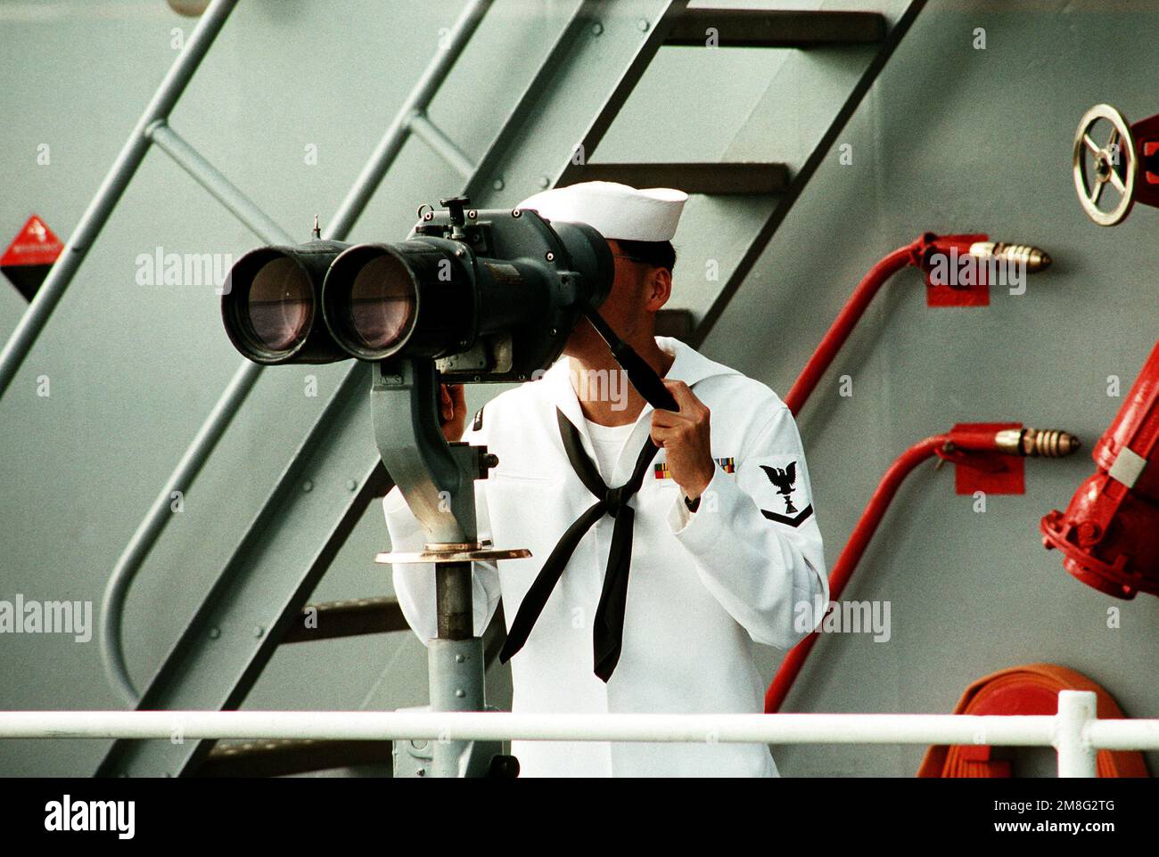 A sailor observes the area through ship's binoculars aboard the U.S. Navy ship. Base: Naval ...