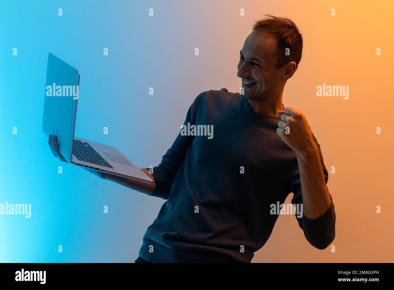 Emotional young man with laptop celebrating victory on color background ...