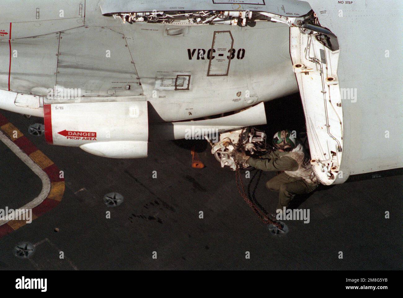 A flight deck crewman attaches tie-down chains to a Fleet logistic ...