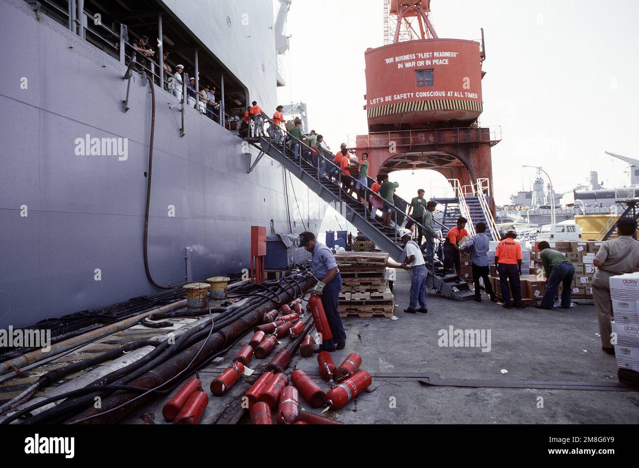 Dock workers load supplies onto the amphibious cargo ship USS DURHAM ...