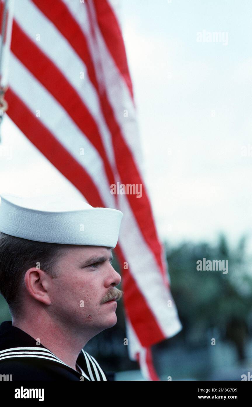 A sailor stands beside the national ensign on the stern of the frigate ...