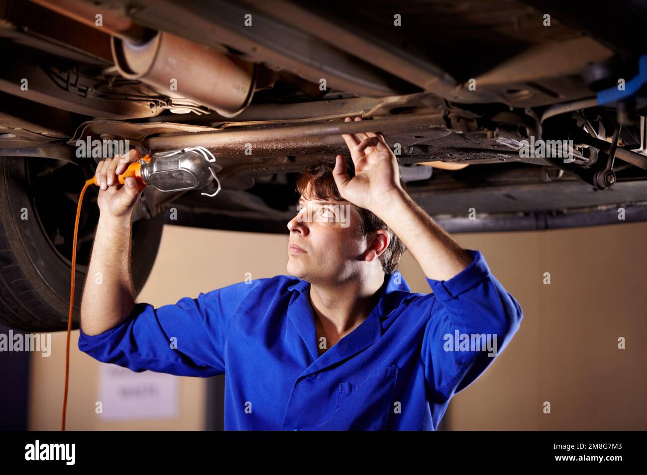 Getting a better look. A young male mechanic looking underneath a car ...