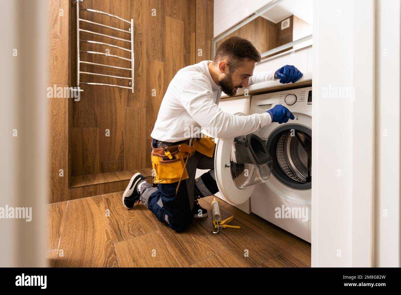 Plumber in overalls with tools is repairing a washing machine in the ...