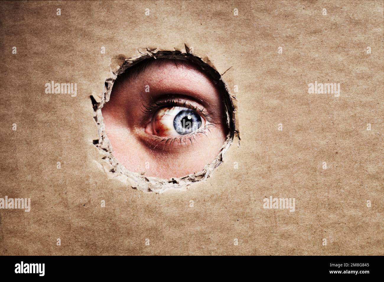 Through the looking hole. Closeup of an eye looking through a hole in a ...