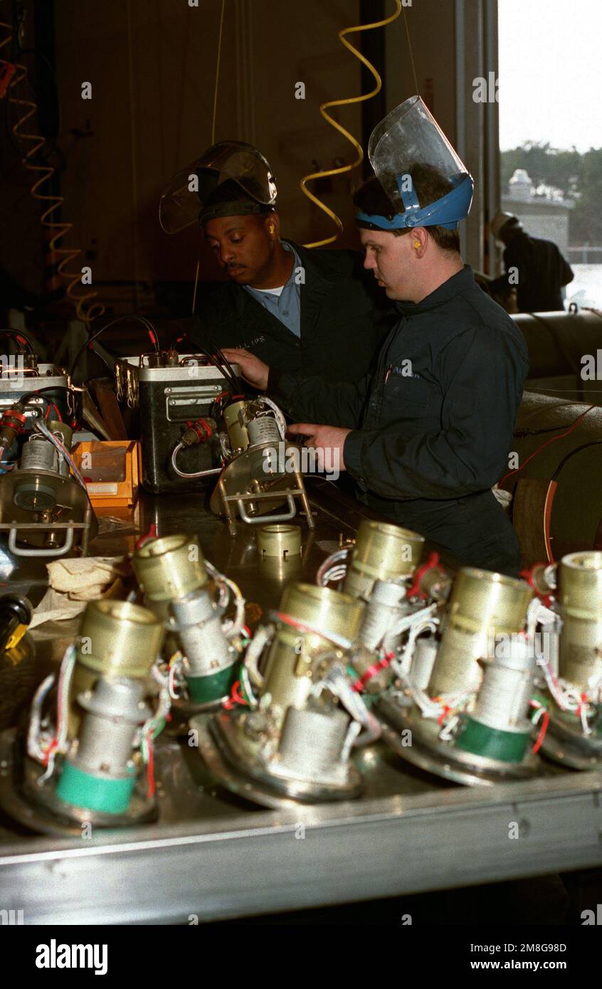 Two minemen use instruments to check mine firing mechanisms on a mine ...
