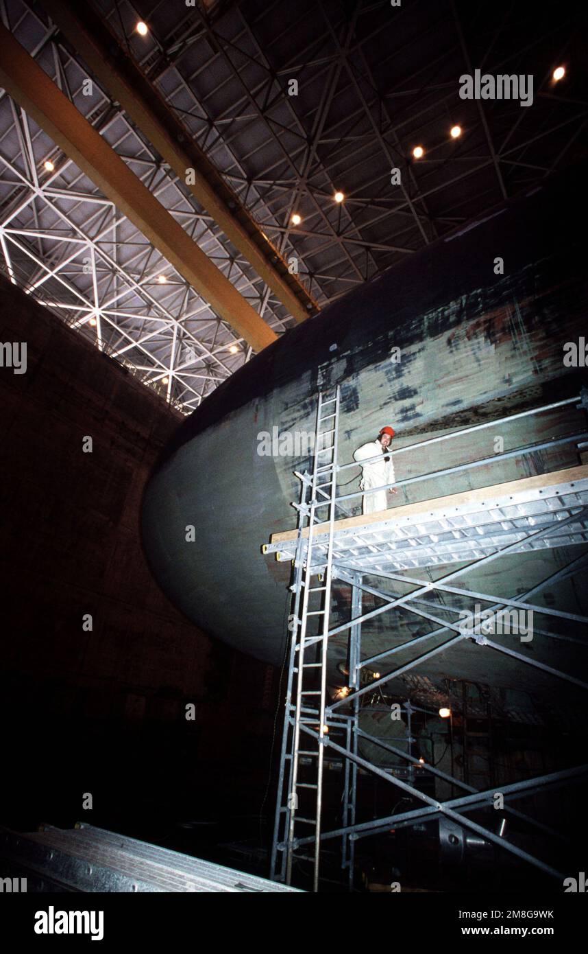 A technician on scaffolding examines the hull of the nuclear-powered ...