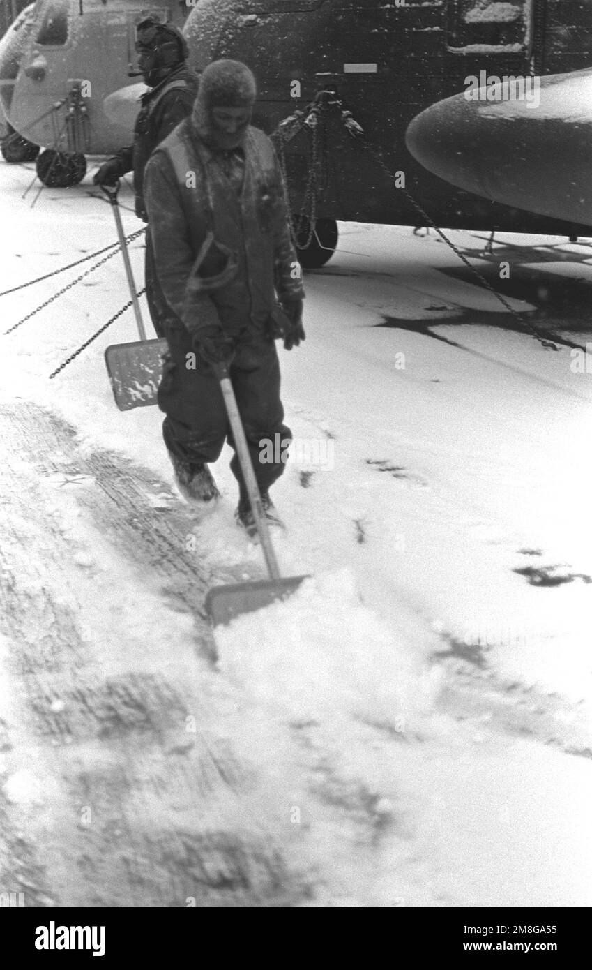 Crewmembers in cold weather dress shovel snow from the flight deck of ...