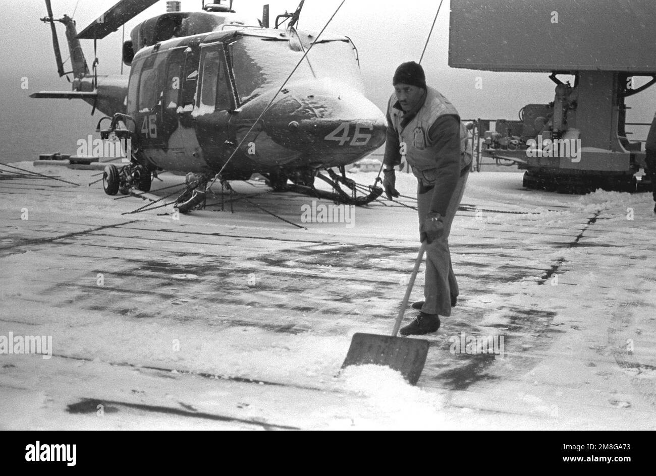 A crew member shovels snow from the flight deck of the amphibious ...