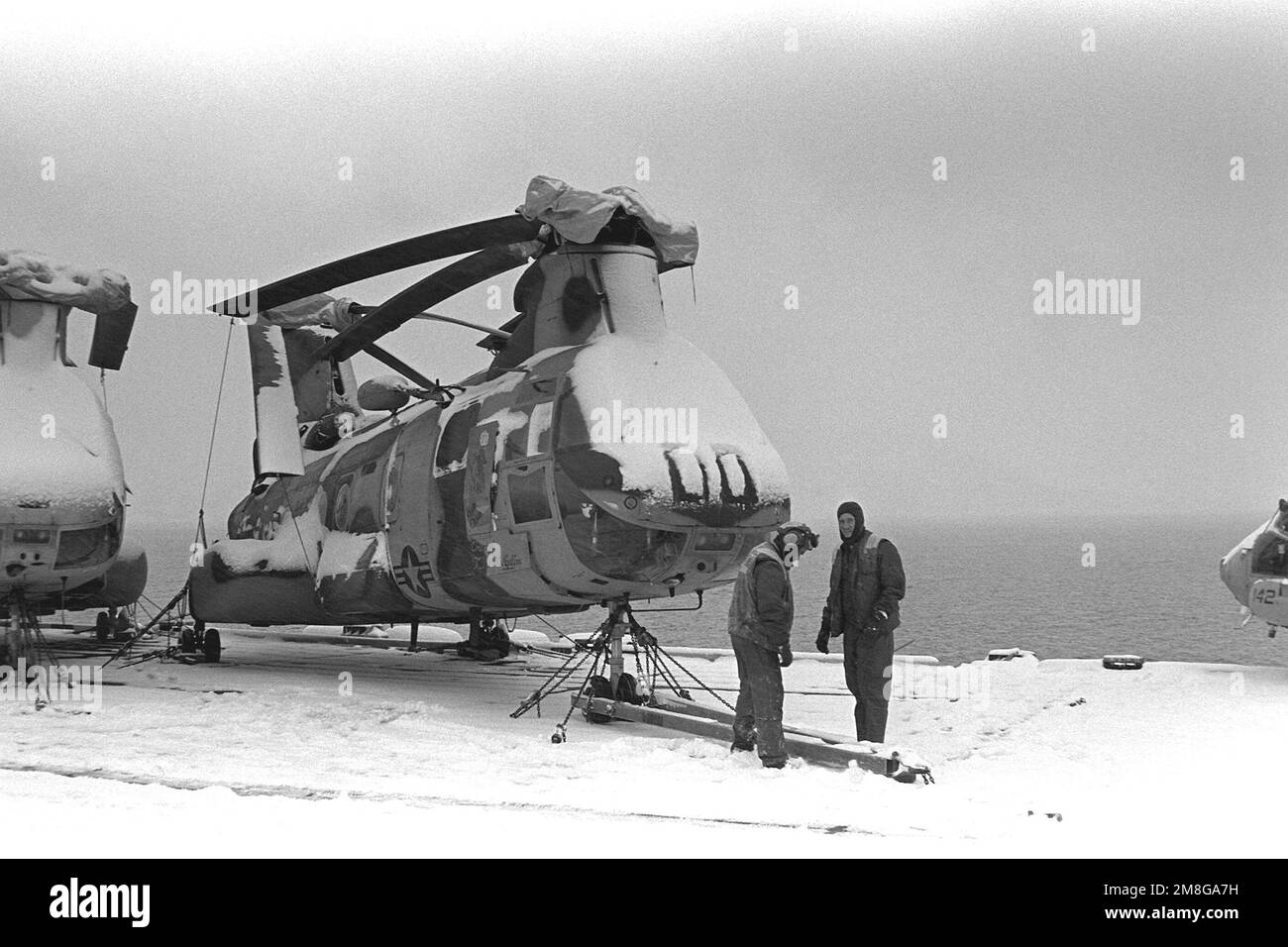 Flight deck personnel attach a tow bar to the front of a CH-46E Sea ...
