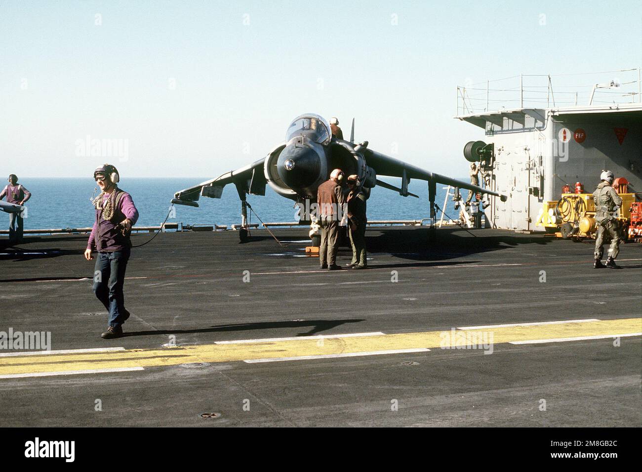 Flight deck crew members stand near an AV-8B Harrier aircraft aboard ...