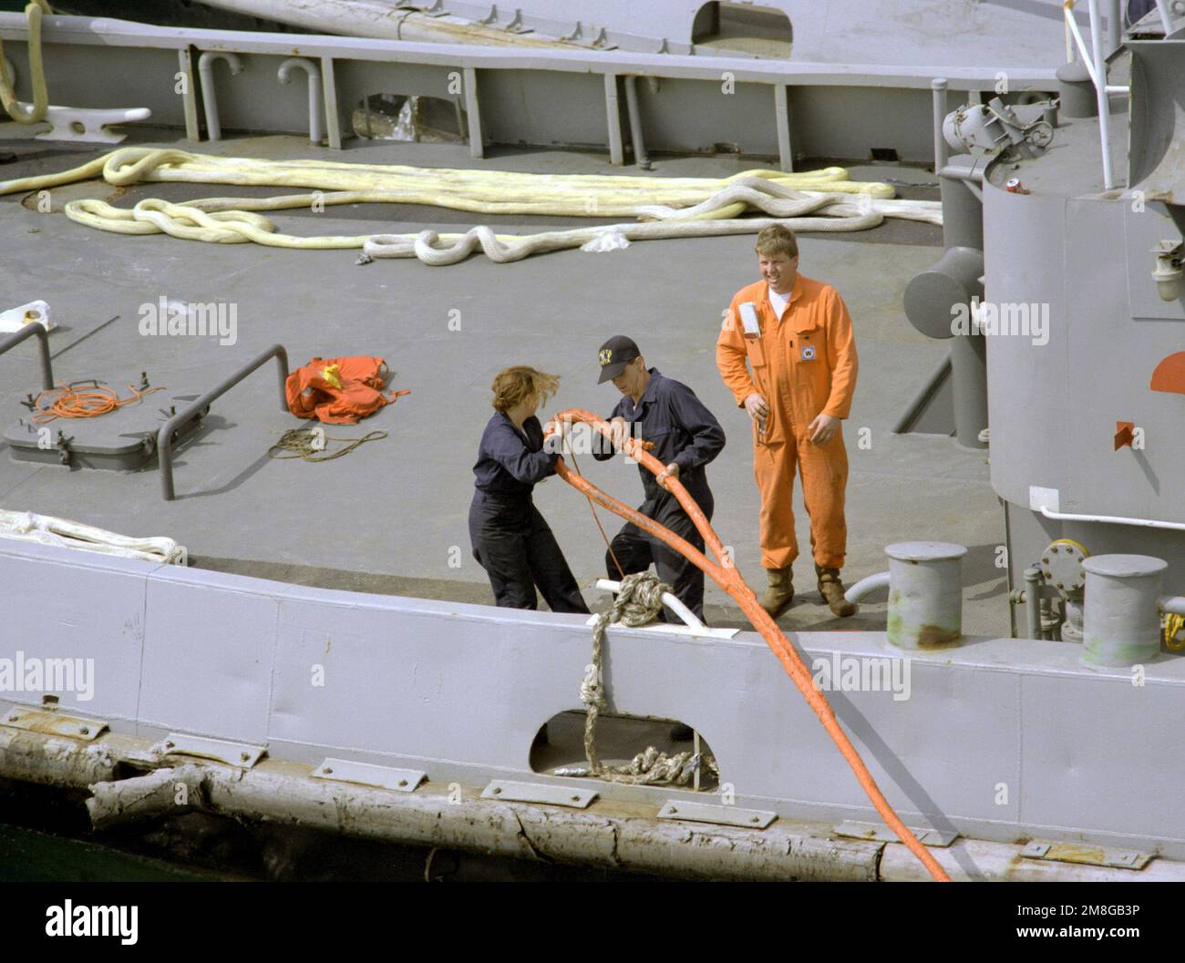 Crew mbembers haul a mooring line aboard while positioning a large ...
