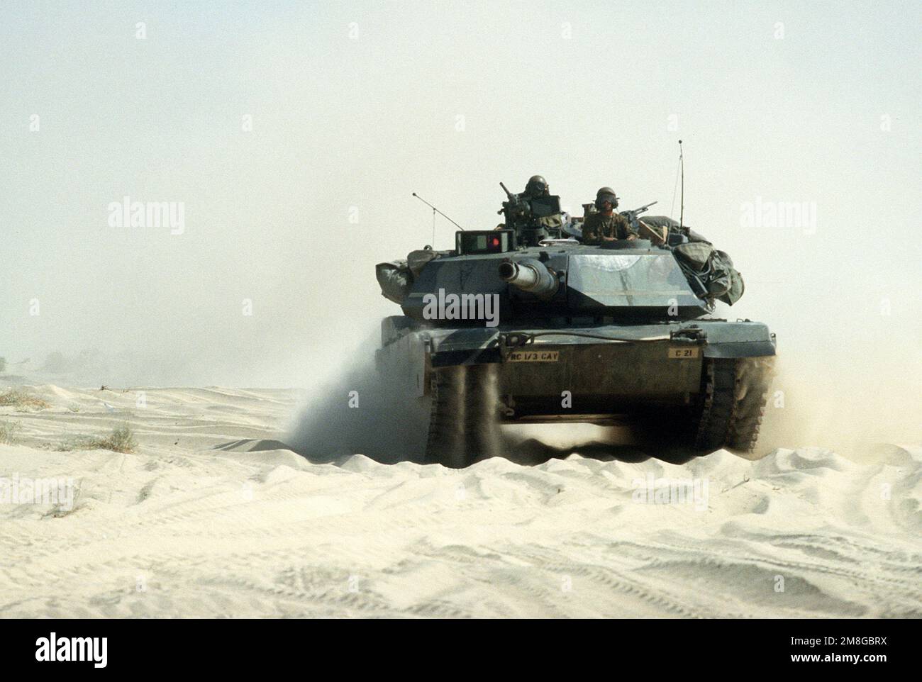 An M-1A1 Abrams main battle tank travels with a convoy on a desert road ...