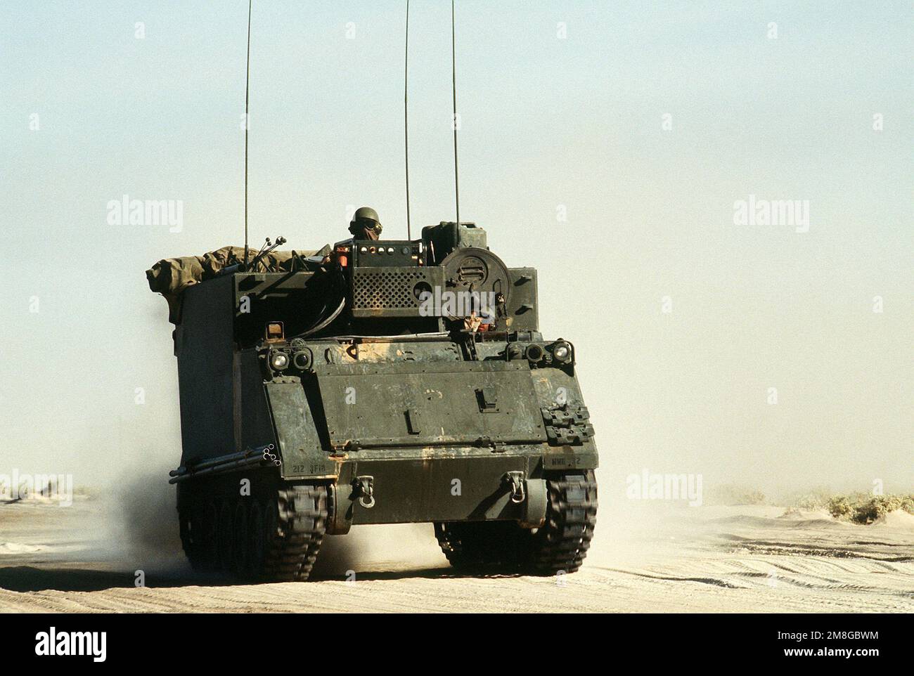 An M-577 armored command vehicle travels with a convoy on a desert road ...
