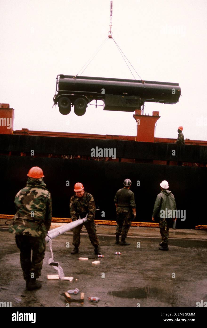 Cargo handlers stand by on the pier as a water tank is lifted by crane ...
