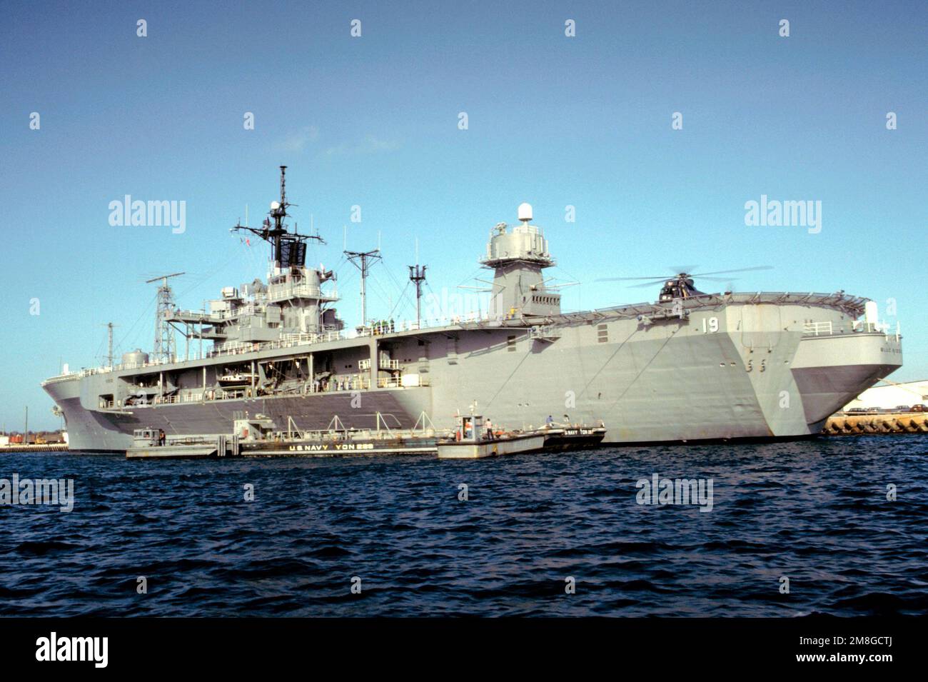 A fuel barge is anchored alongside the amphibious command ship USS BLUE ...