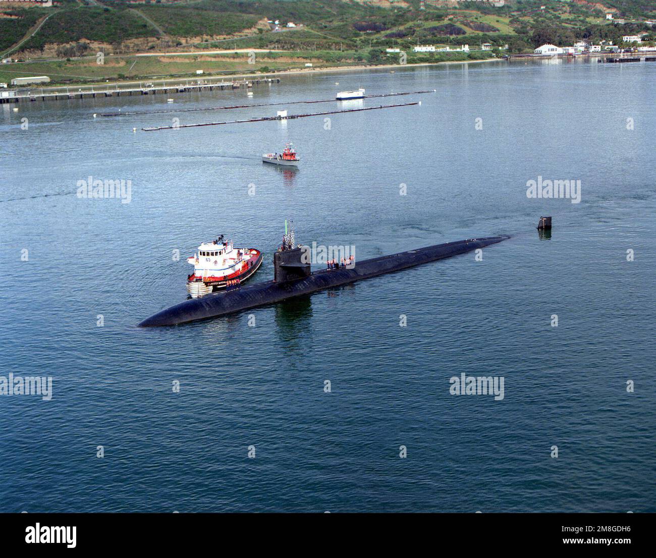A tug assists a Los Angeles class nuclear-powered attack submarine away ...