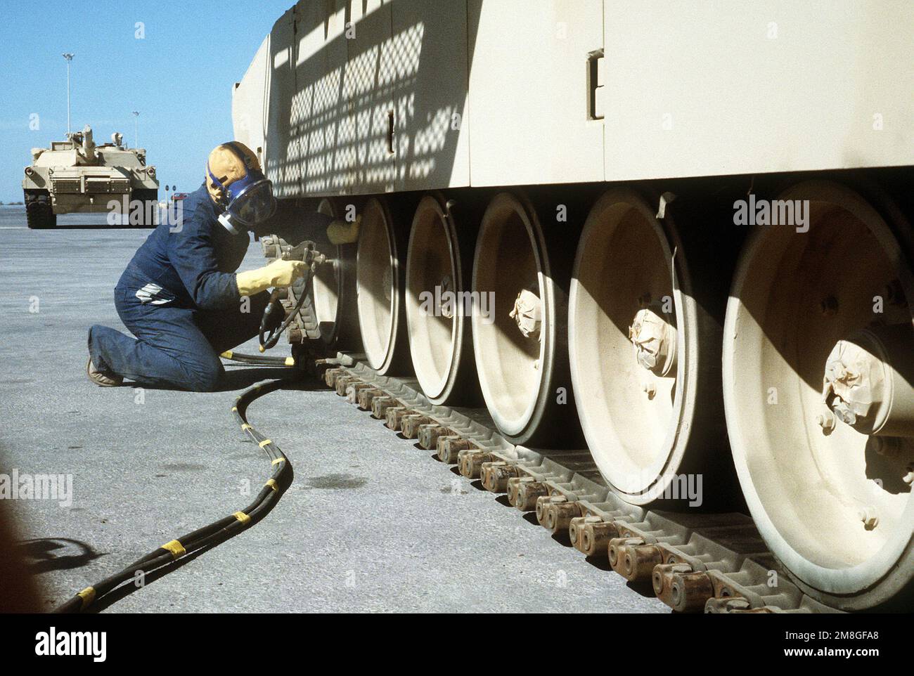 A civilian employee paints desert camouflage colors on an M-1A1 Abrams ...