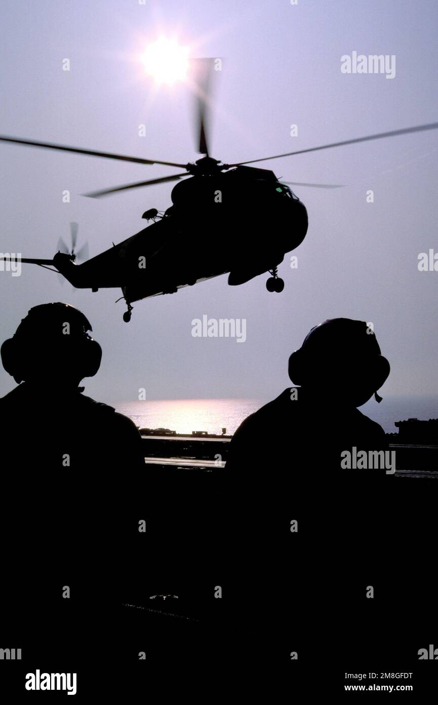 A silhouette of flight deck crew members watching as a Helicopter Anti ...