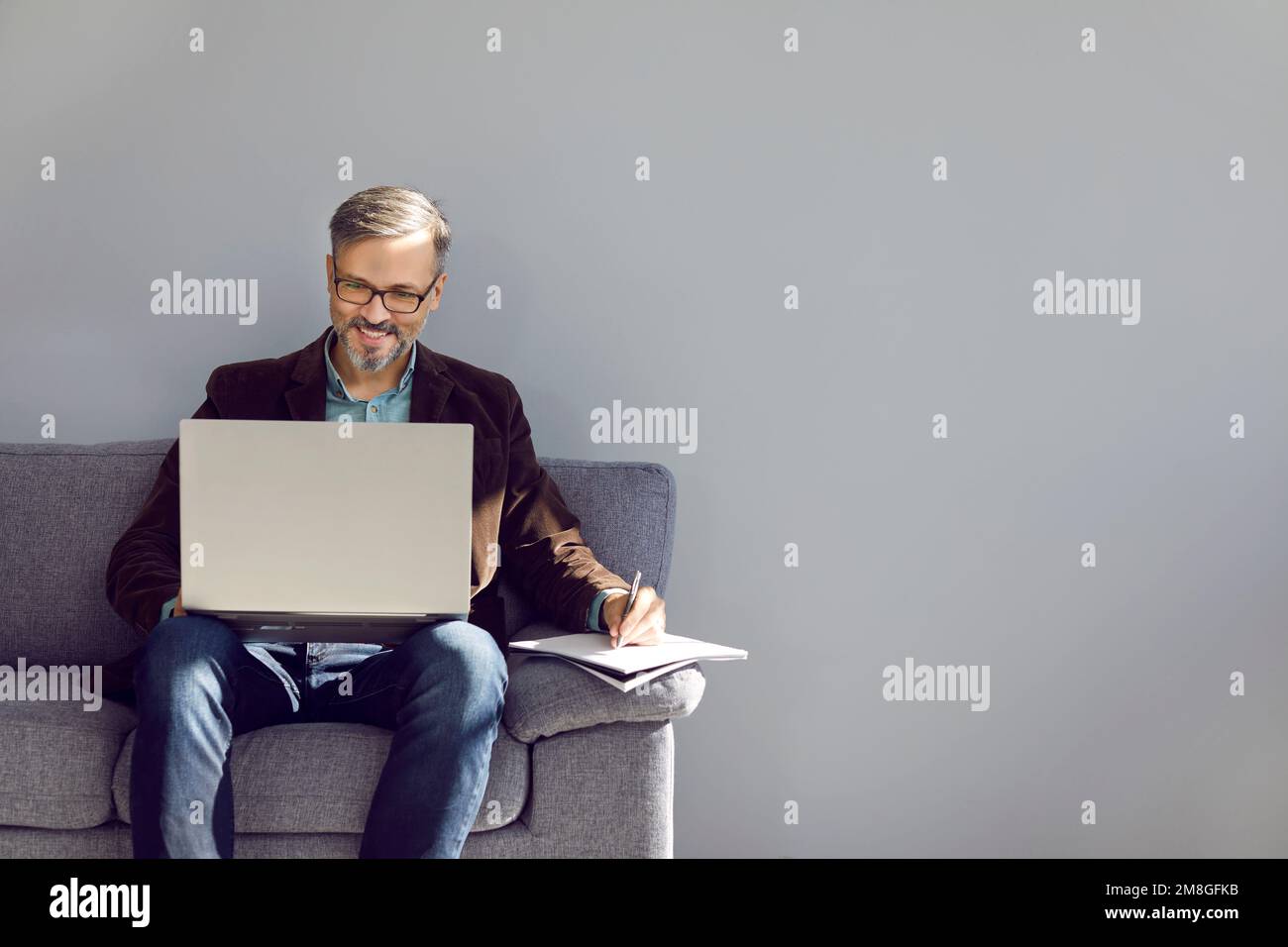 Happy mature businessman using laptop computer while sitting on couch ...