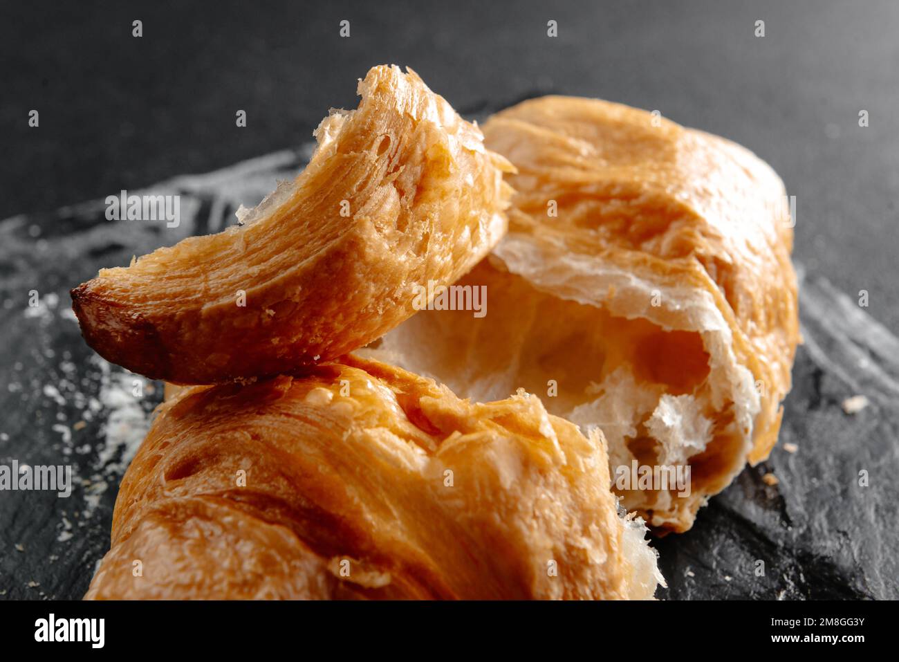 Close-up of croissants on a dark background. One croissant broken into ...