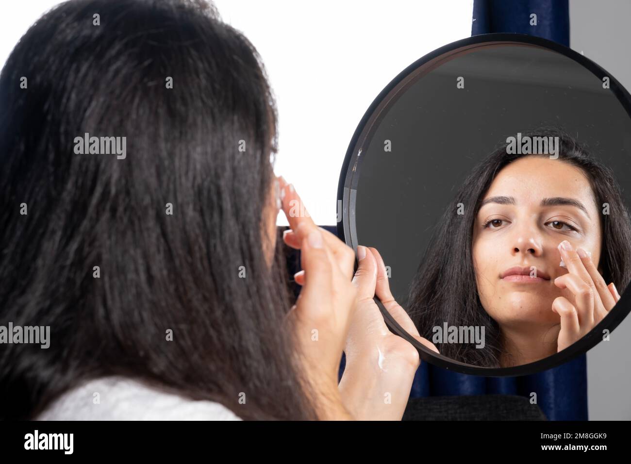 Over shoulder back view of 30s lady applying cream. Looking and holding ...