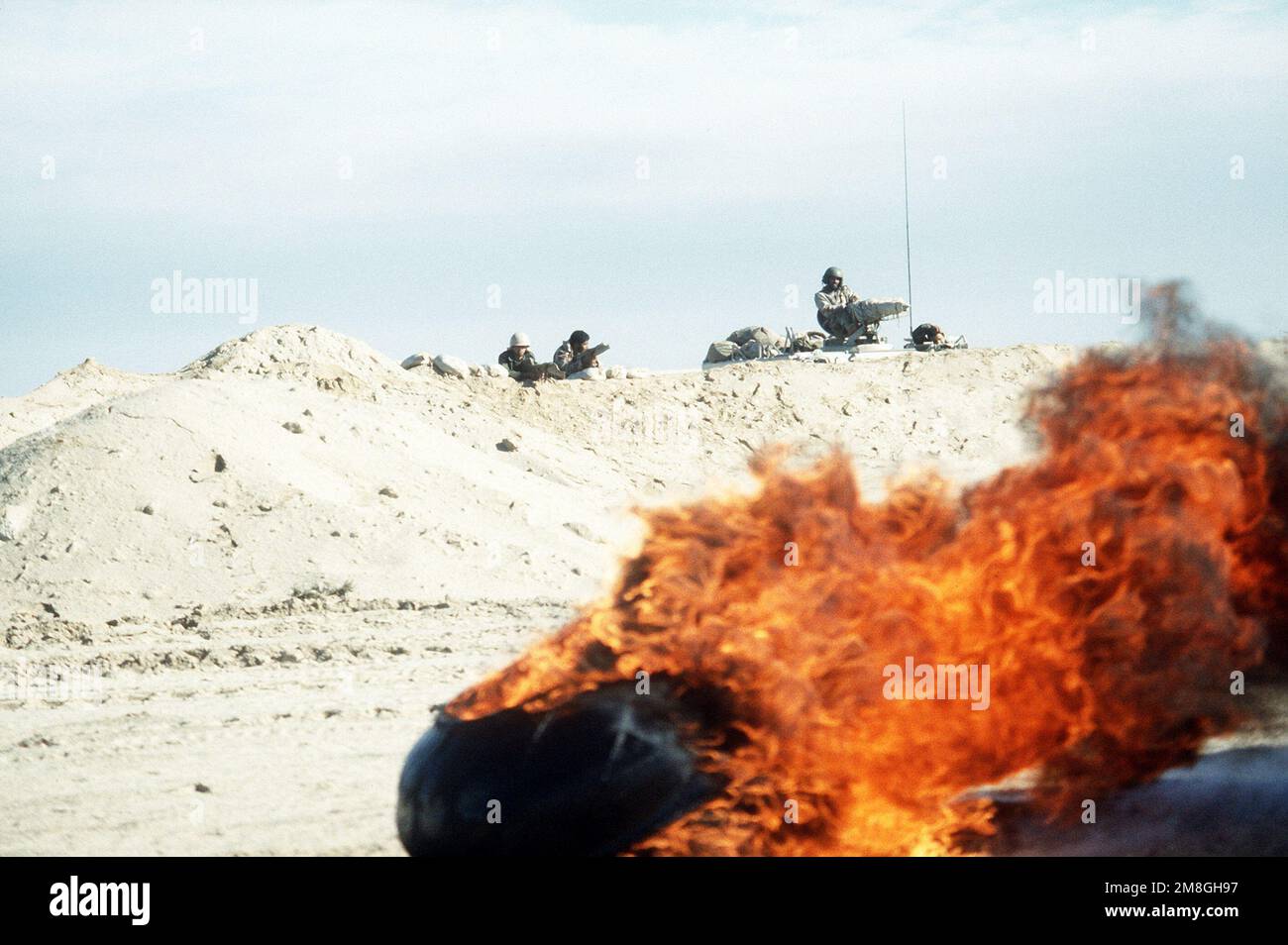 Armed military personnel watch over a berm as a fire burns in the ...