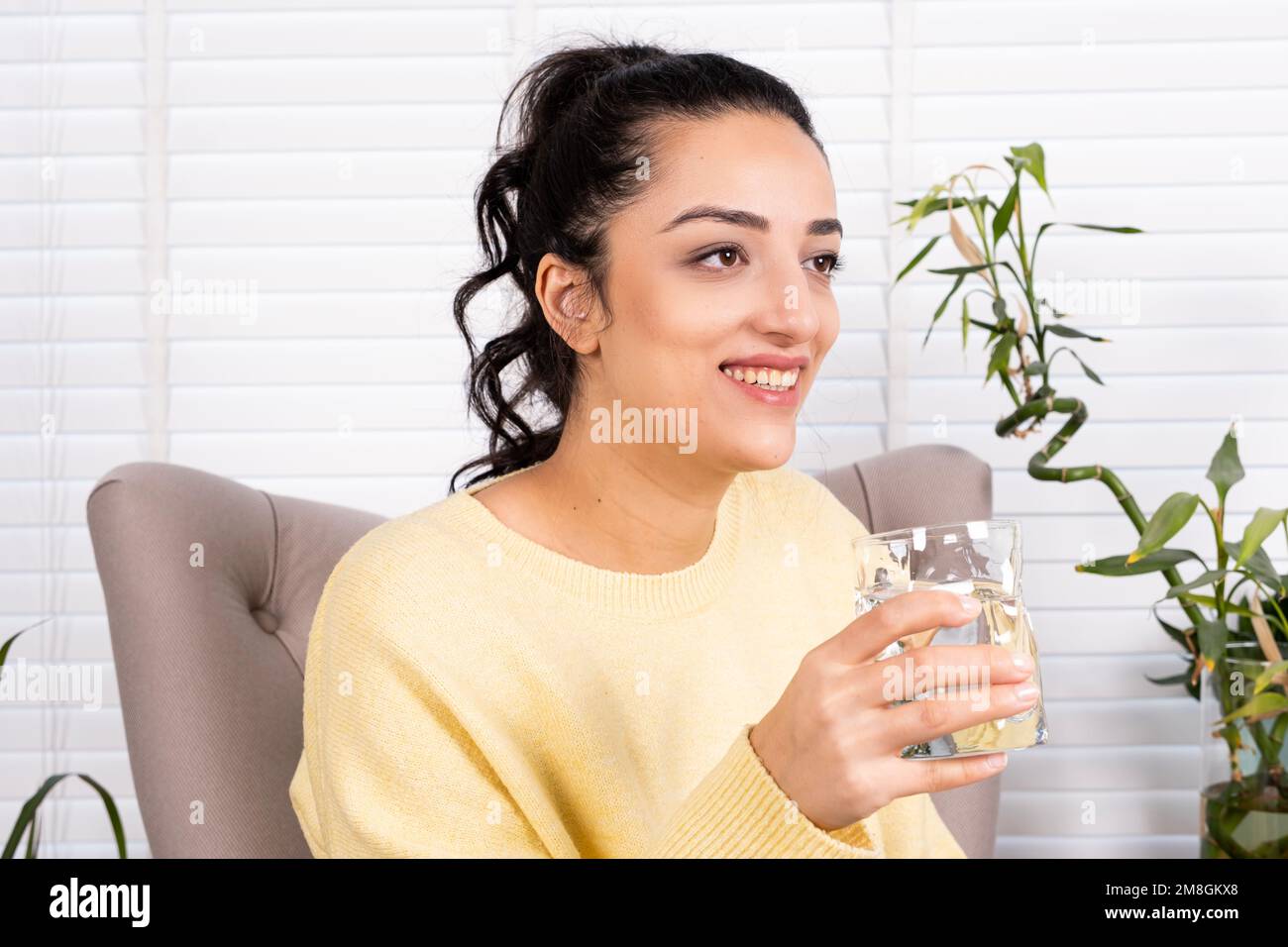 Smiling young woman holding glass of pure water. Looking aside, happy ...