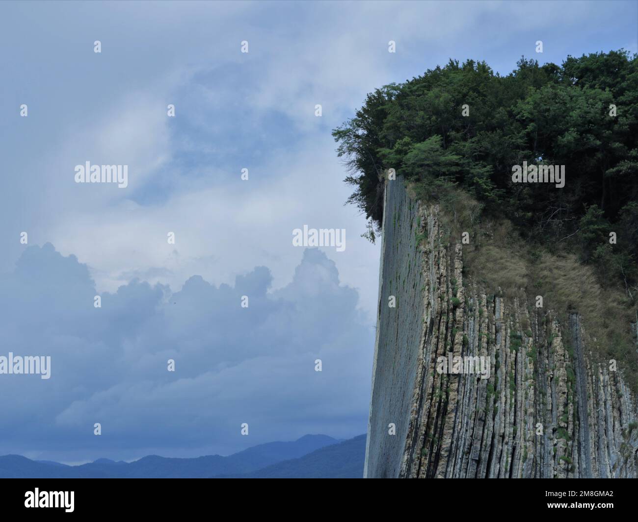 high steep cliff with layered texture and green vegetation on top ...