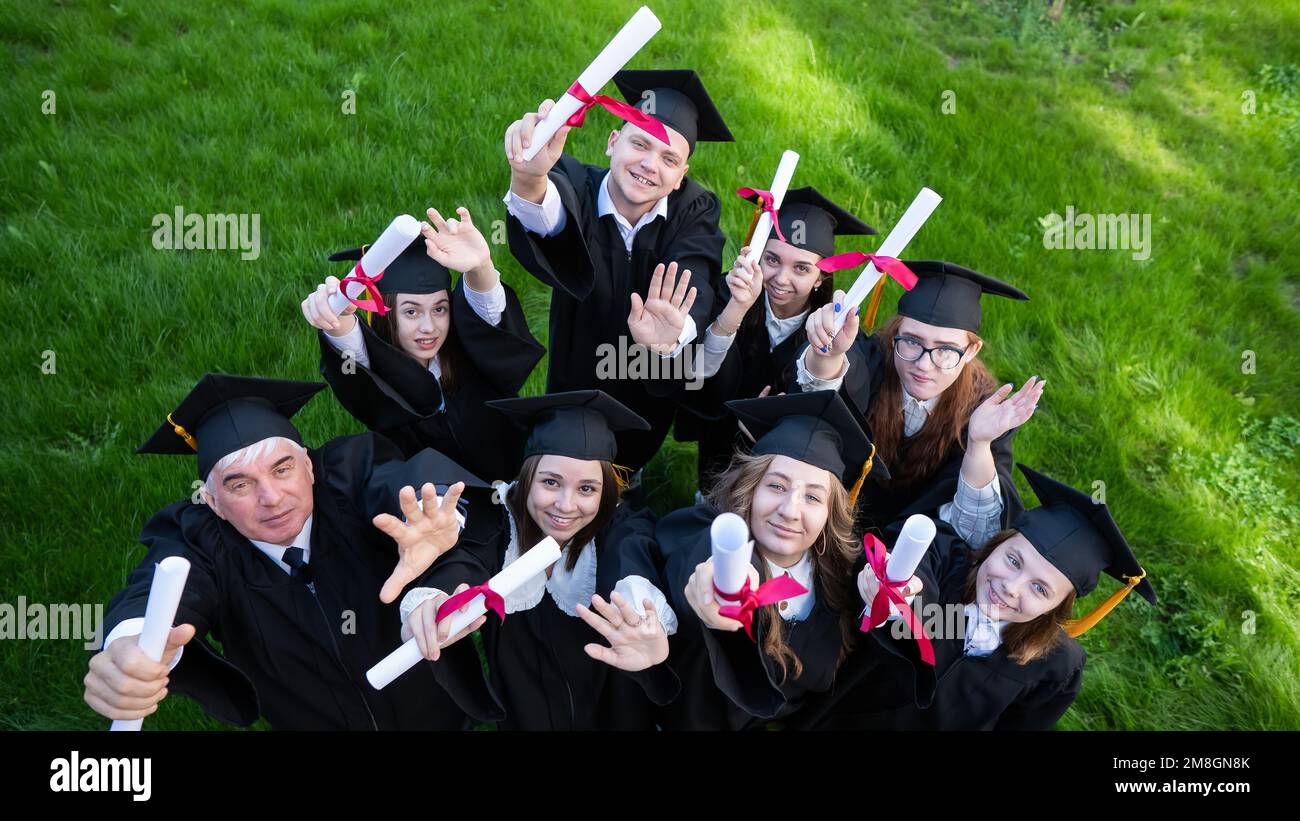 Graduates in robes show off their diplomas outdoors. View from above ...