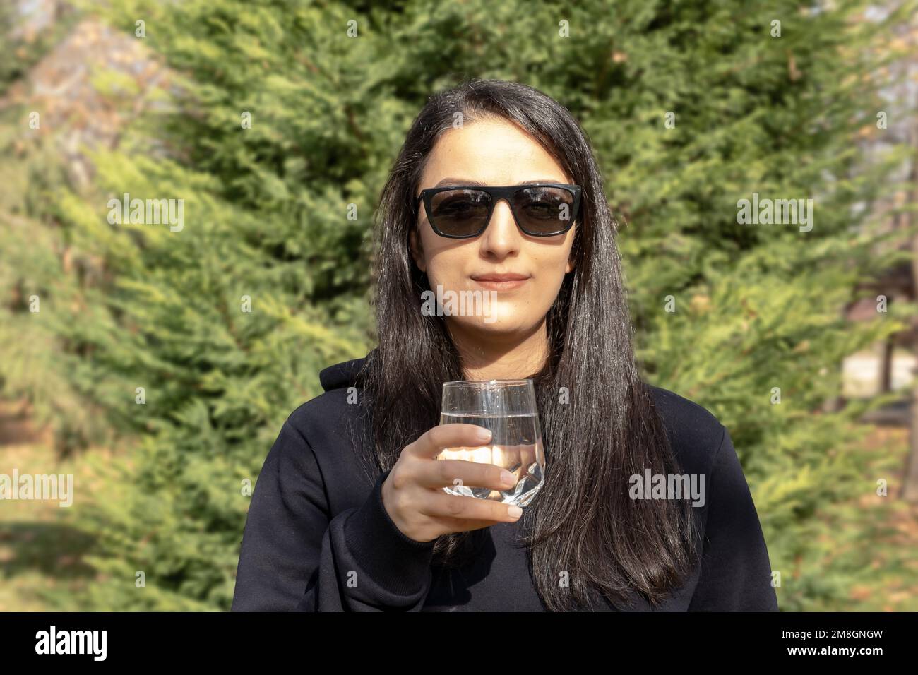 Holding glass of water. Millennial girl standing outdoor at the park ...